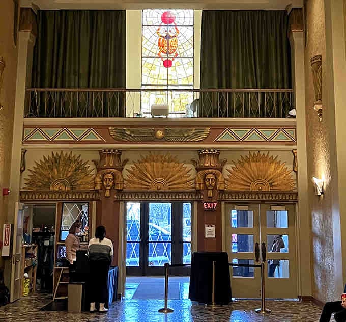 Patrons gather beneath stained glass and Egyptian deities, blending everyday moments with extraordinary surroundings.