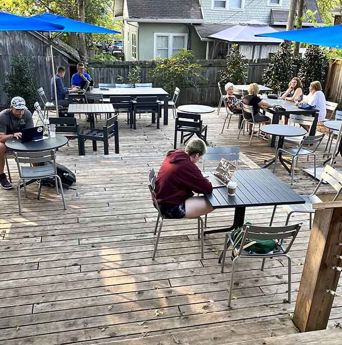 Blue umbrellas shade the wooden deck where coffee tastes better outdoors, surrounded by fences and fellow caffeine enthusiasts relaxing.