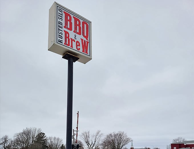 The roadside sign stands tall like a lighthouse guiding hungry travelers to their smoky, saucy salvation below.