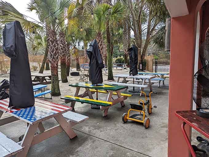 The outdoor patio features colorful picnic tables under swaying palms, creating the perfect spot for al fresco tropical dining.