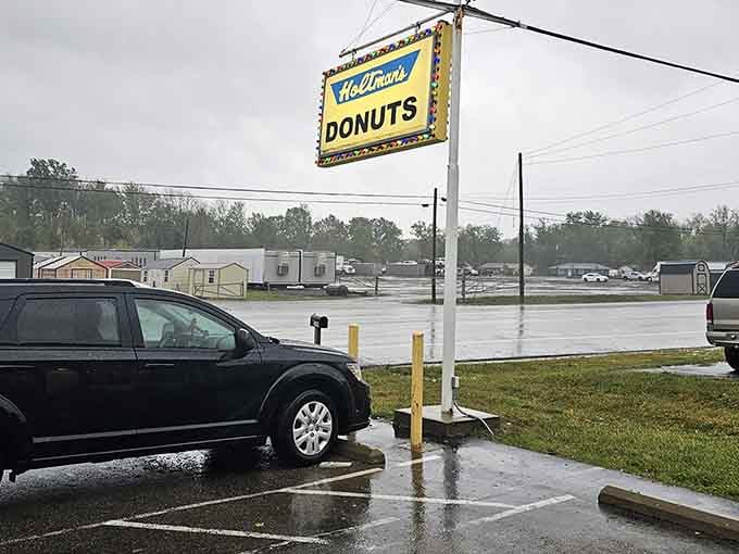 The parking lot on a wet morning, where cars gather like pilgrims at a shrine dedicated to fried dough excellence.