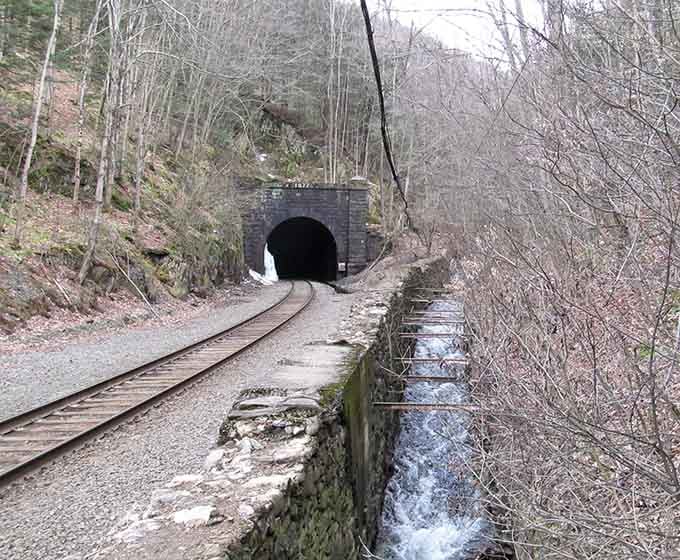 Railroad tracks disappear into blackness that swallowed nearly 200 lives during construction, a sobering historical reality.