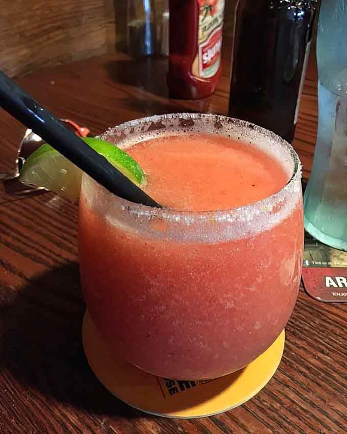 A frozen strawberry margarita with a salted rim that looks like summer tastes, perfectly blended and dangerously drinkable.