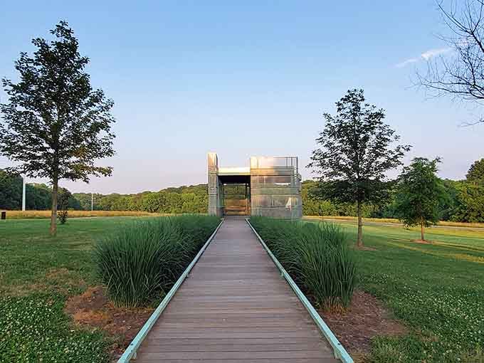 A wooden walkway leads to a glass pavilion rising from the landscape like a modern temple to art and contemplation.