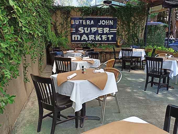 The charming outdoor patio features vintage signage and greenery, offering al fresco dining that feels like a secret garden escape.