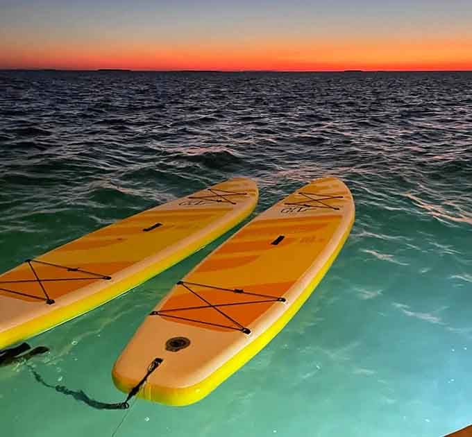 Paddleboards waiting for adventure as the sun paints the sky in colors that make artists weep with envy.