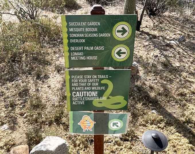 Directional signs point toward specialized gardens while friendly rattlesnake warnings remind visitors to respect desert wildlife boundaries.