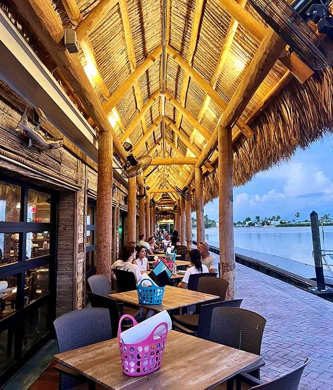 Waterfront patio seating with those massive wooden posts and palm thatch overhead delivers unobstructed views that make every meal feel special.