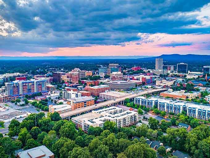 Mountains meet modern living where green trees frame colorful buildings that stretch toward those dramatic purple-tinged clouds above.