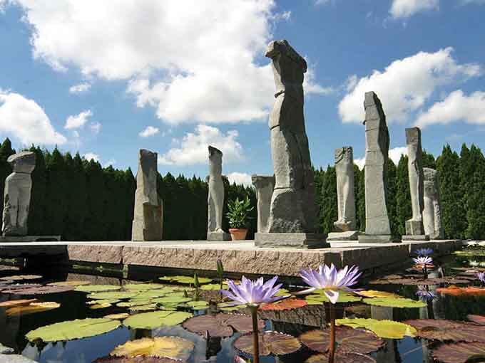 Ancient stone columns rise beside purple water lilies, creating a scene that feels like discovering Atlantis in your own backyard.