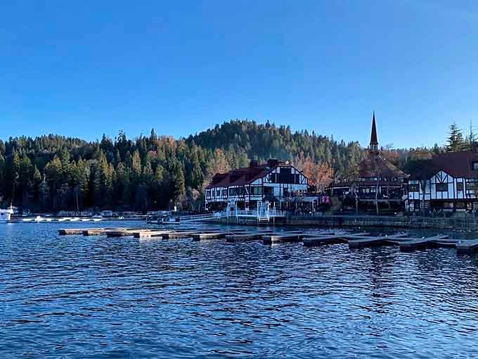 Alpine charm meets mountain lake serenity where Tudor-style buildings reflect in crystalline waters beneath towering pines.