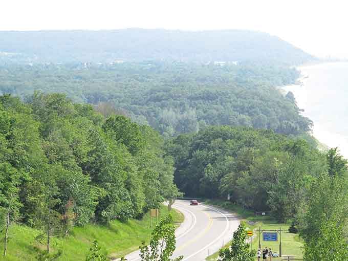 Where the road curves like a gentle ribbon, lush green hills meet shimmering Lake Michigan in perfect harmony.