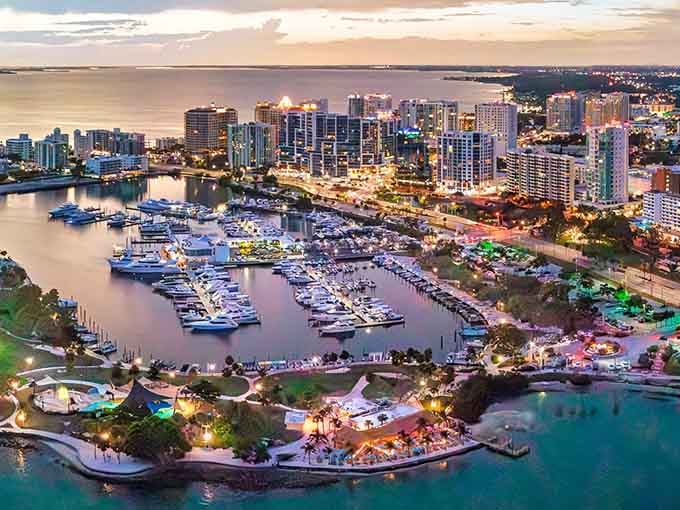 The marina comes alive as evening approaches, with lights beginning to twinkle across buildings that hug the peaceful shoreline.