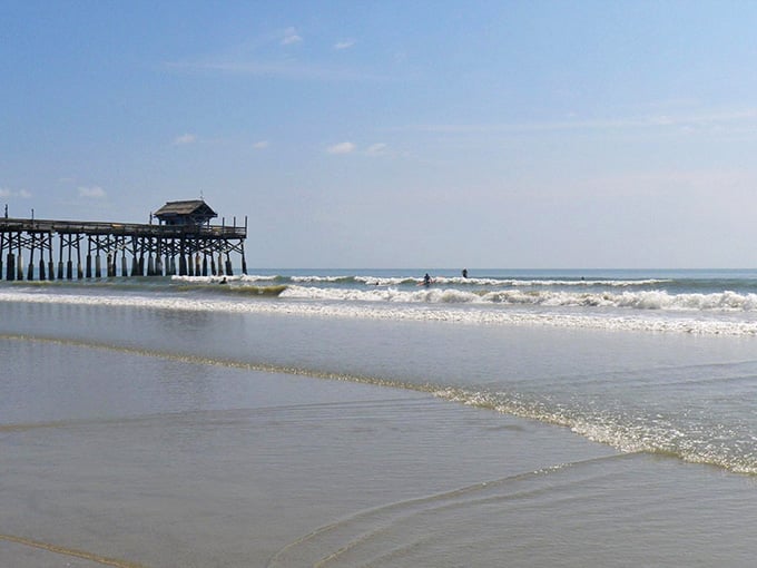 Surfers catching waves while the historic pier watches over them like a proud wooden grandfather.