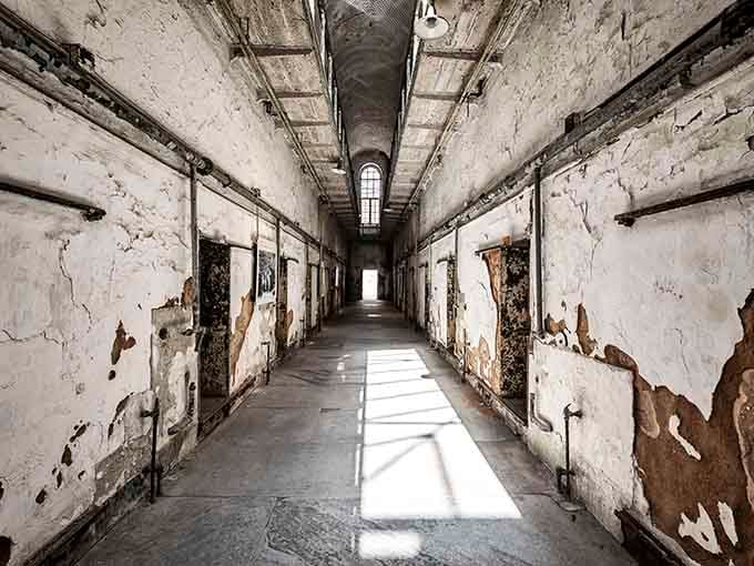 Sunlight streams through barred windows, casting shadows that dance across crumbling walls like ghosts refusing to leave their posts.