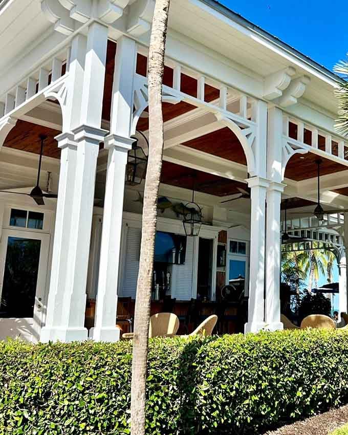 Crisp architectural details frame the entrance where island breezes meet elegant dining under swaying palms and blue skies.