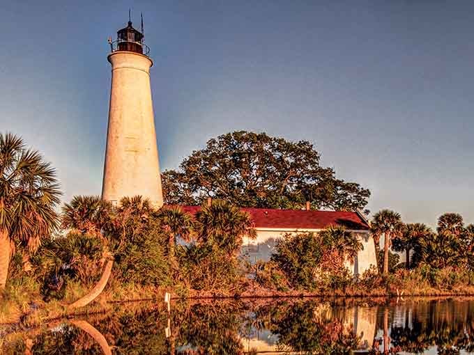 The lighthouse's reflection dances in still waters while palm trees frame this peaceful scene like a postcard from old Florida.