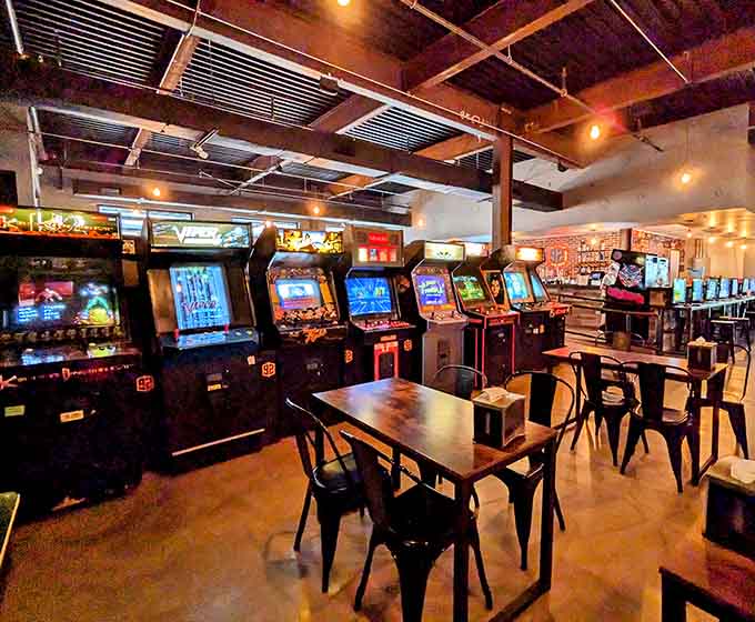 Industrial chic meets neon nostalgia in a space where exposed beams frame rows of glowing arcade cabinets perfectly.