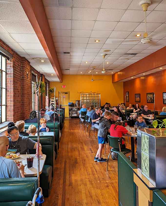 Bright walls, green booths, and exposed brick create the kind of welcoming atmosphere where strangers become regulars without even trying.