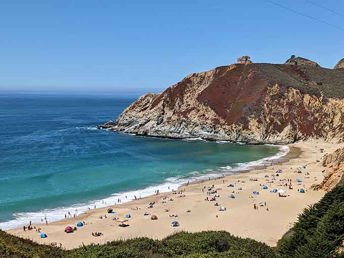 Beach umbrellas dotting the sand like colorful confetti against those magnificent striped cliffs behind them.