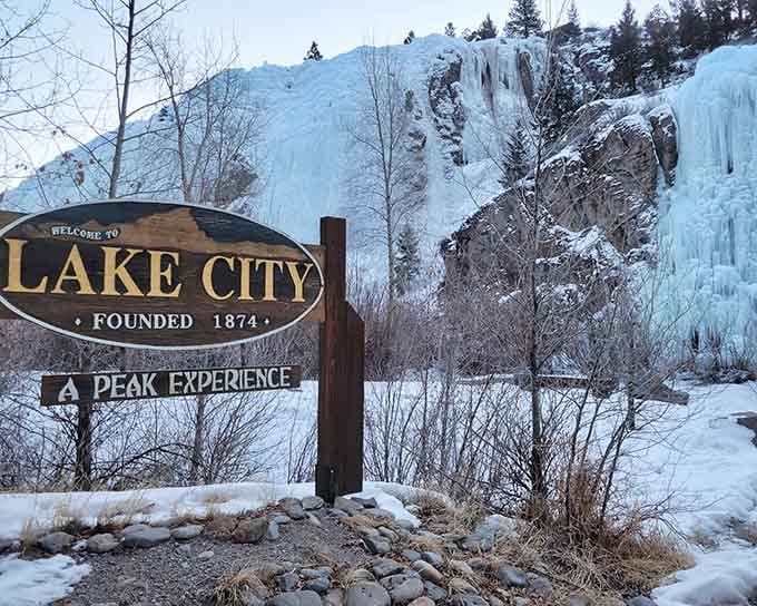 Winter's frozen waterfalls frame this welcome sign like nature's own ice sculpture garden, promising adventures beyond your wildest dreams.