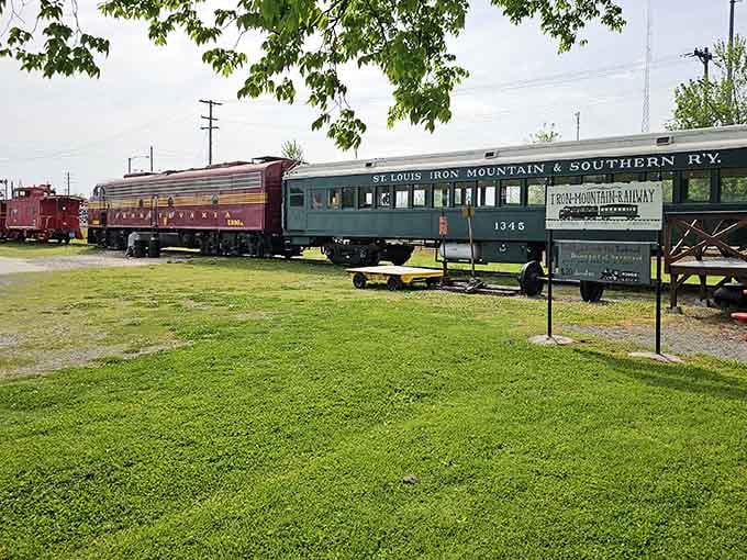 Historic railway cars rest peacefully on manicured grass, their colorful paint jobs telling stories of bygone railroad glory.
