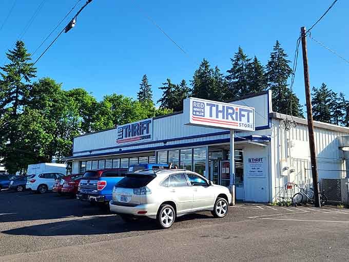 The Red White & Blue sign sits proudly under towering evergreens, promising patriotic savings and vintage finds galore.