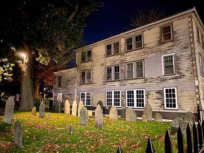 Ancient gravestones lean like crooked teeth beside weathered colonial buildings, marking where innocent lives were tragically lost.
