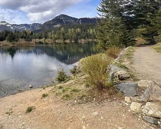 Crystal-clear pond waters mirror snow-capped peaks perfectly, creating a view so stunning you'll think someone Photoshopped reality.