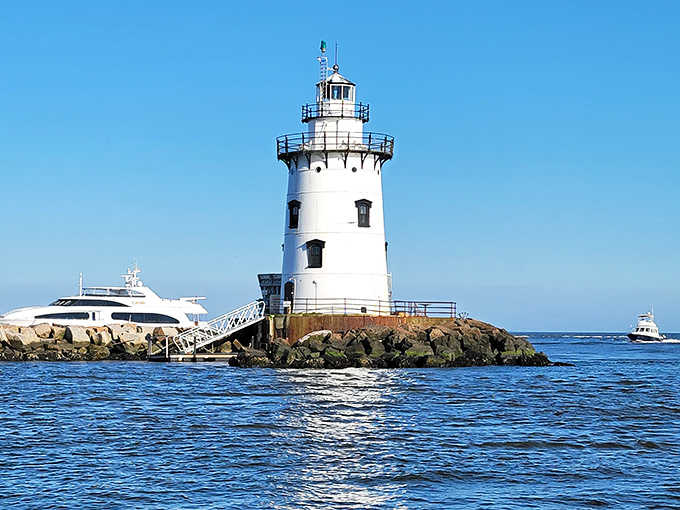 Modern yachts cruise past this timeless guardian, proving some things never go out of style or usefulness.