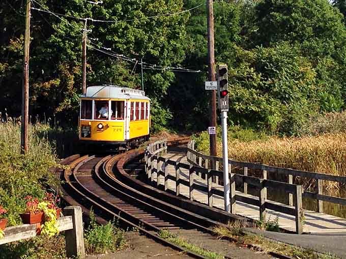 The vintage trolley curves gracefully along the tracks, framed by autumn grasses and overhead power lines that tell stories.