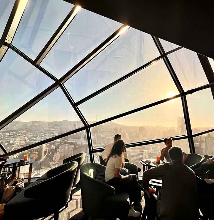 Sunset through geometric glass creates a cathedral of light above the urban landscape below.