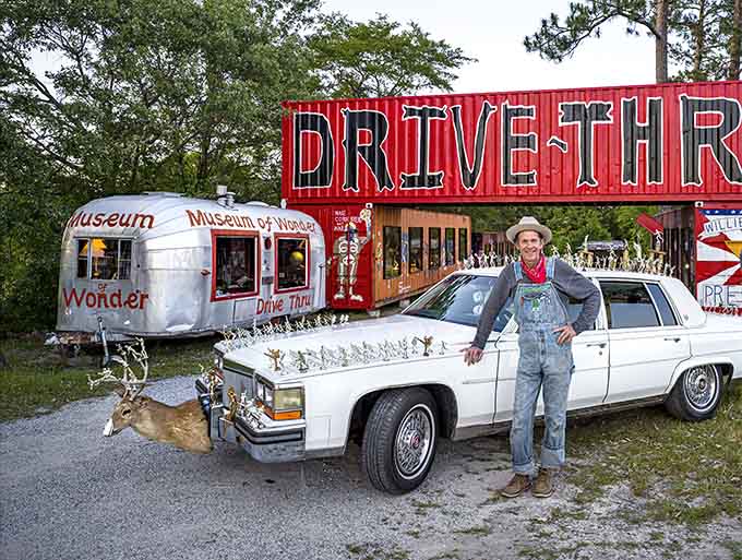 The artist himself stands proudly beside his creation, a vintage Cadillac adorned with enough hood ornaments for a parade.