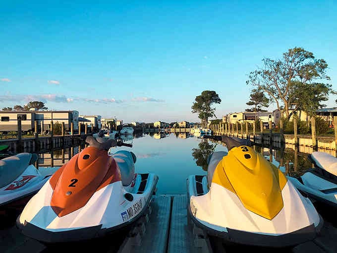 Jet skis waiting patiently by the water like colorful horses ready to gallop across liquid pastures at dawn.