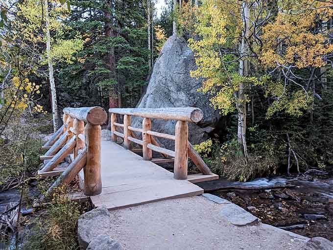 This log bridge spans the creek in autumn, framed by golden aspens and a distinctive pointed boulder.