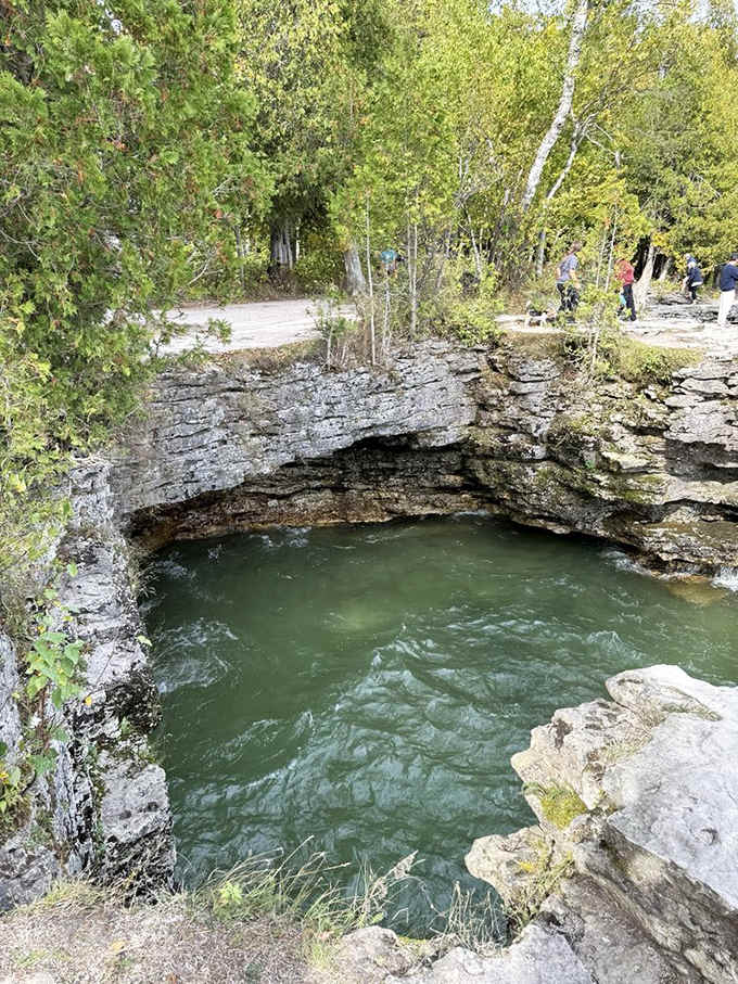 Nature's swimming pool gleams emerald green beneath weathered limestone cliffs, inviting contemplation and wonder from above.