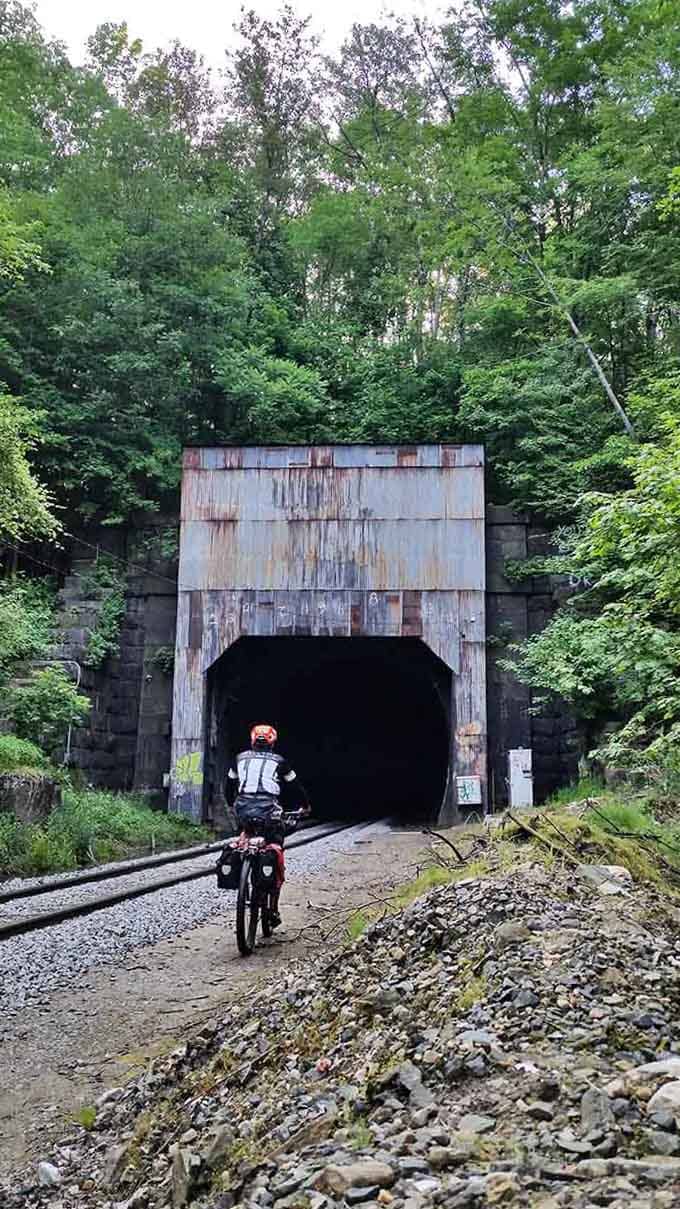 This rusty tunnel entrance yawns like a giant's mouth, swallowing brave cyclists into its mysterious depths.