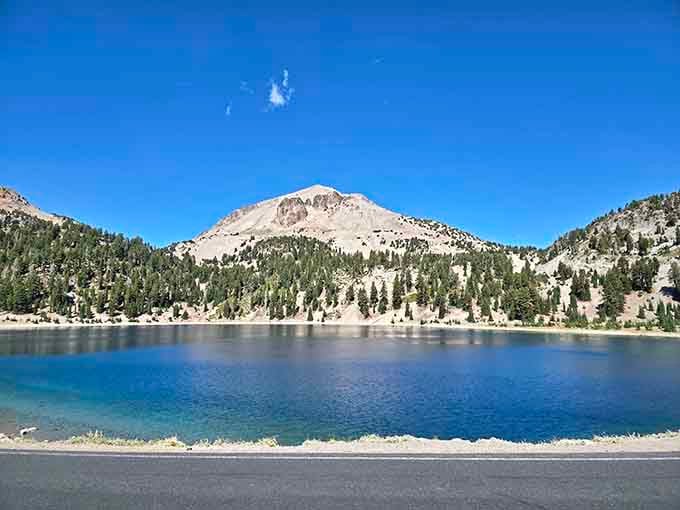 That impossibly blue alpine lake reflects snow-capped peaks like a mirror polished by the mountain gods themselves.