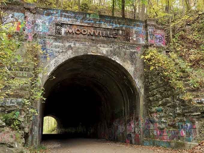 Graffiti-covered bricks frame this dark portal where railroad history meets modern urban art in the woods.