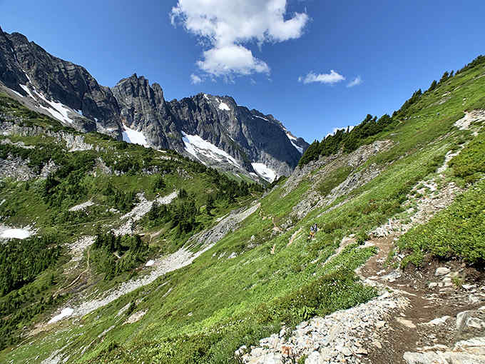 Brilliant blue skies frame rugged granite peaks where patches of snow cling stubbornly even as summer meadows flourish below.