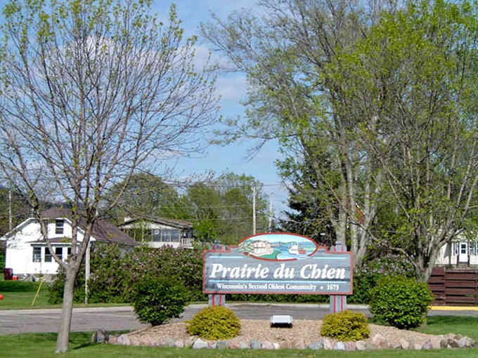 That welcome sign sits surrounded by spring greenery, promising a town where your neighbors actually wave back.