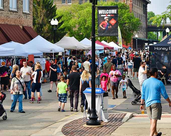 Downtown streets buzz with energy as families stroll past vendor tents on a perfect summer evening together.