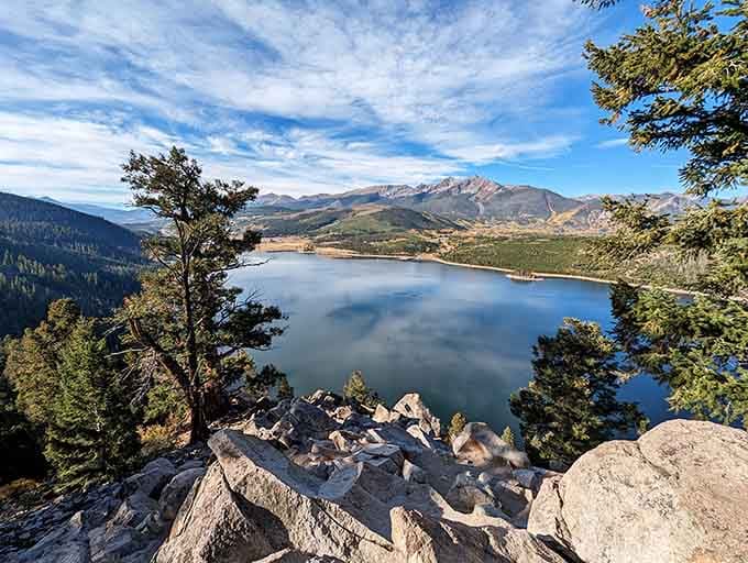 That mirror-perfect reflection transforms this mountain reservoir into nature's own postcard, framed by ancient pines and rocky overlooks above.