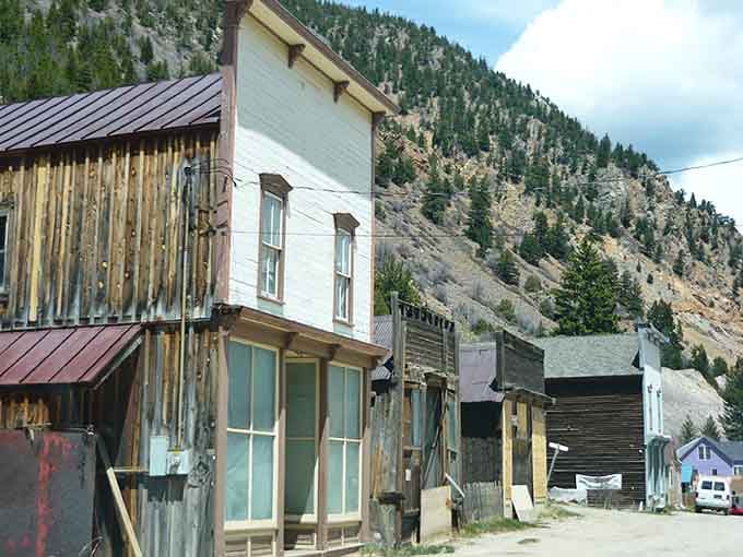 Weathered wooden storefronts stand silent against towering mountain peaks in this perfectly preserved mining town.
