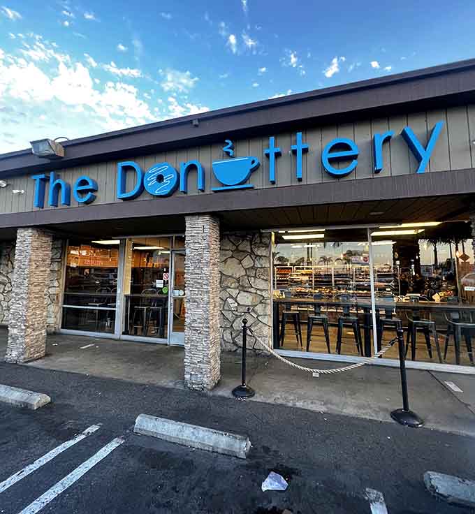 Stone pillars and modern blue lettering create an inviting entrance where fresh donuts emerge throughout the entire day.