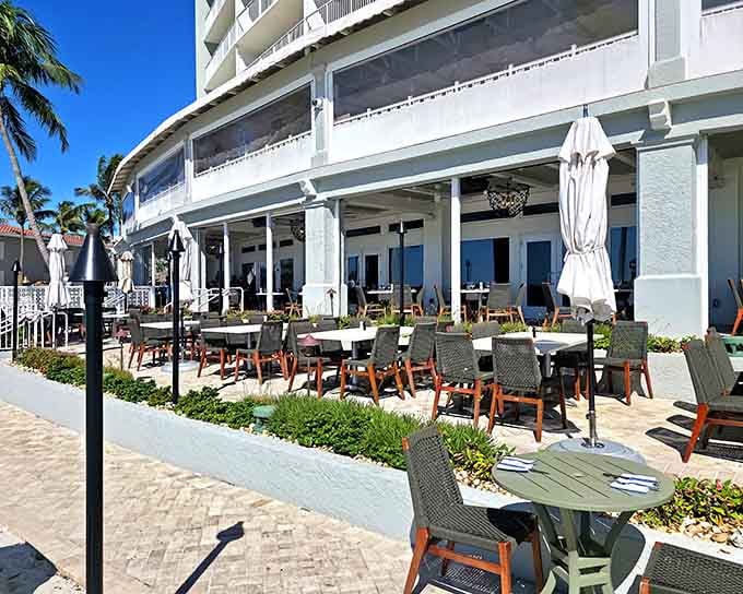 The pristine patio stretches toward endless blue water where Gulf breezes carry the promise of perfectly grilled seafood.