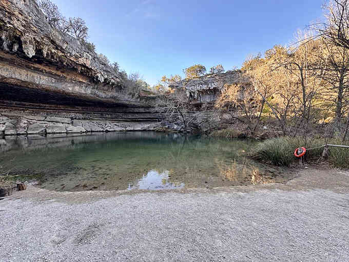 A collapsed grotto reveals jade-green water beneath limestone cliffs, creating nature's own cathedral of cool refreshment.