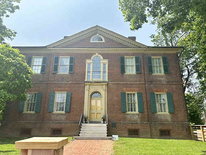 Dappled sunlight filters through ancient trees, casting dancing shadows across this historic home's timeless Federal-style architecture and manicured grounds.