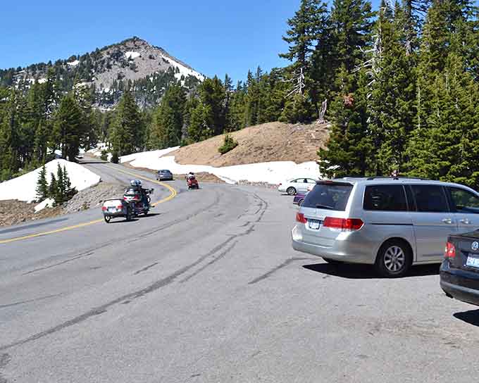 Cars wind through alpine curves where winter and summer shake hands in the same spectacular moment.