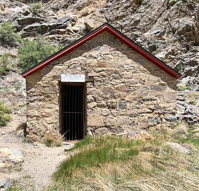 The old stone building with its red-trimmed roof guards secrets carved deep into the mountainside behind it.